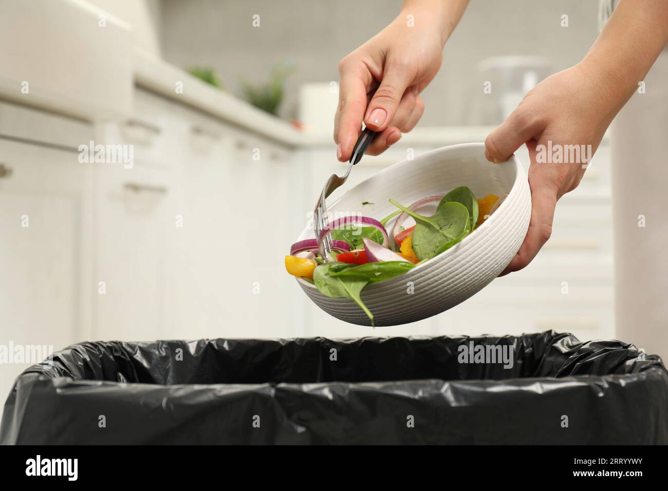 Woman throwing vegetable salad into bin indoors, closeup Stock Photo ...