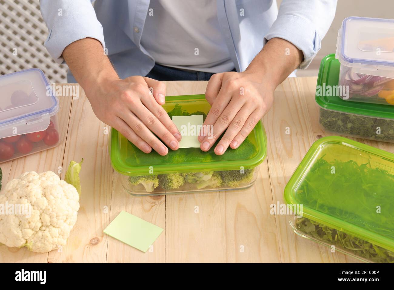 Man sticking paper note onto container with fresh broccoli at wooden ...