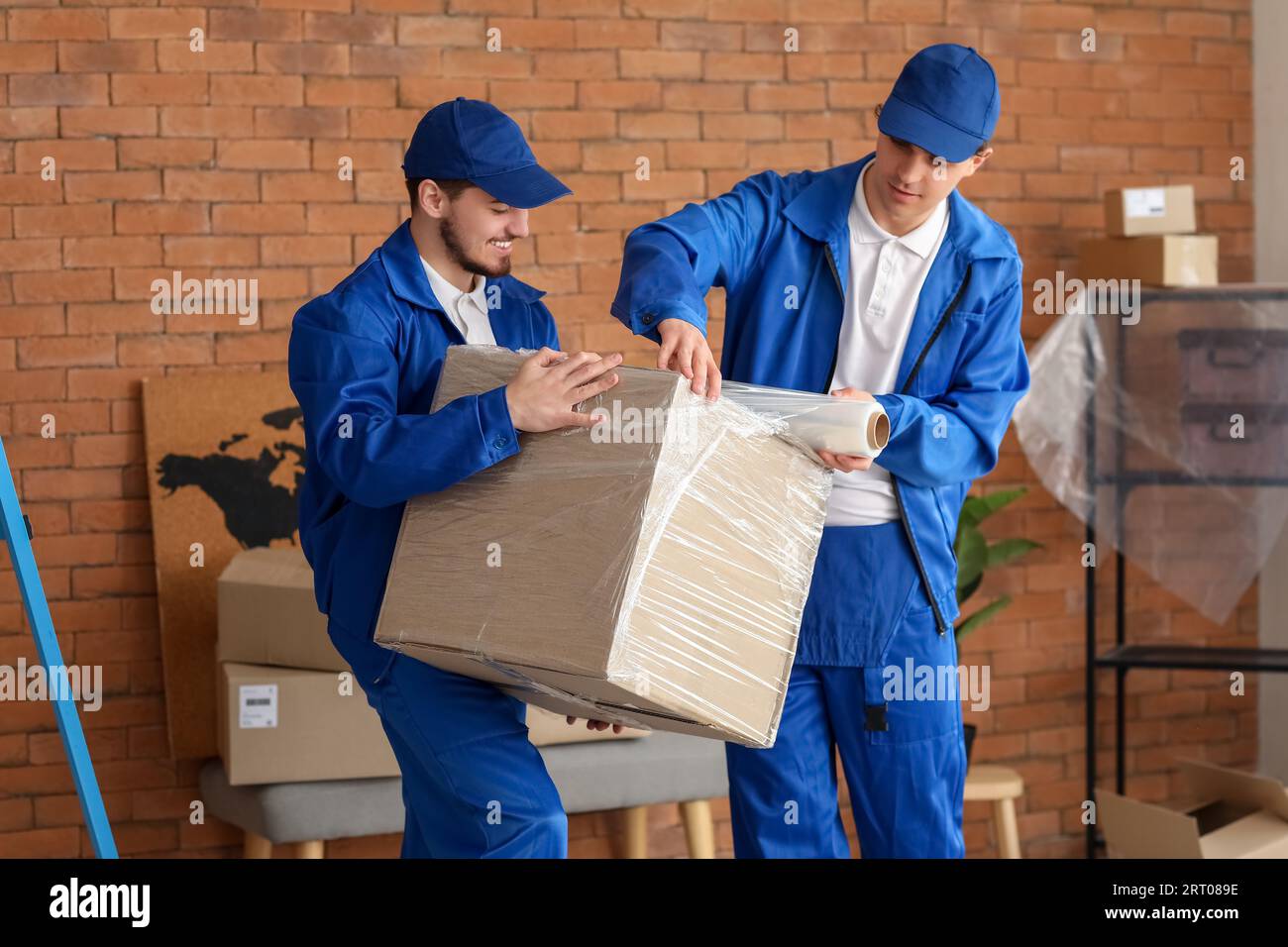 Male movers wrapping box with stretch film in room Stock Photo - Alamy