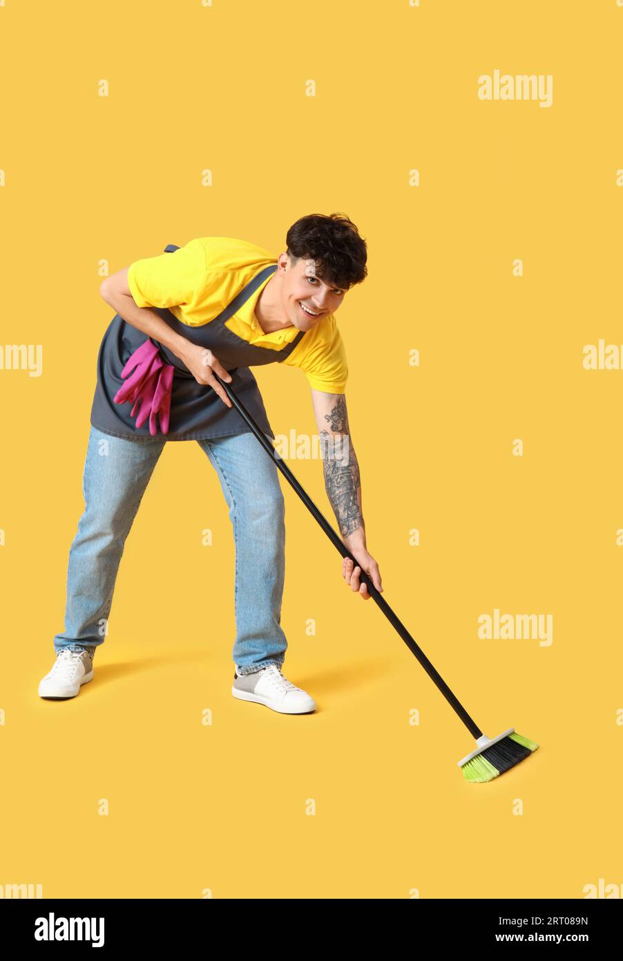 Male janitor with broom on yellow background Stock Photo - Alamy