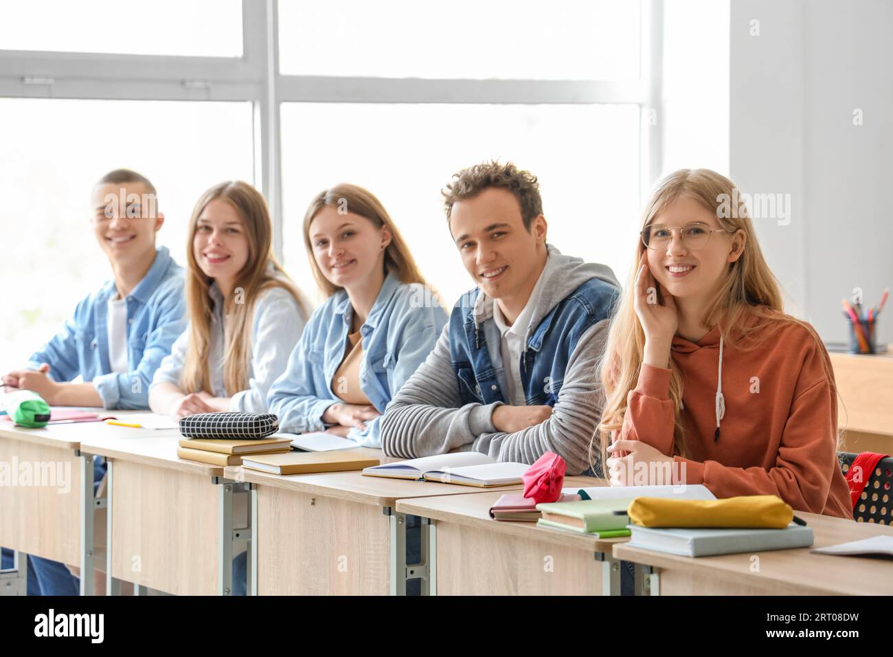 Happy classmates sitting at desks in classroom Stock Photo - Alamy