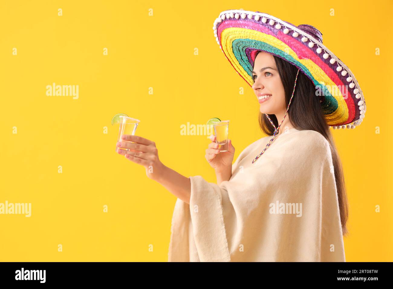 Beautiful young Mexican woman in sombrero and with tequila on yellow ...