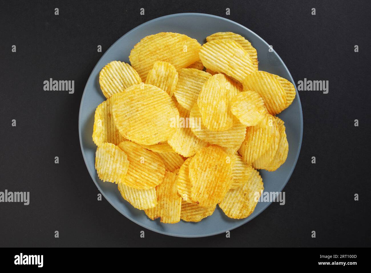 Salty ribbed potato crisps in a gray plate on black background, top ...