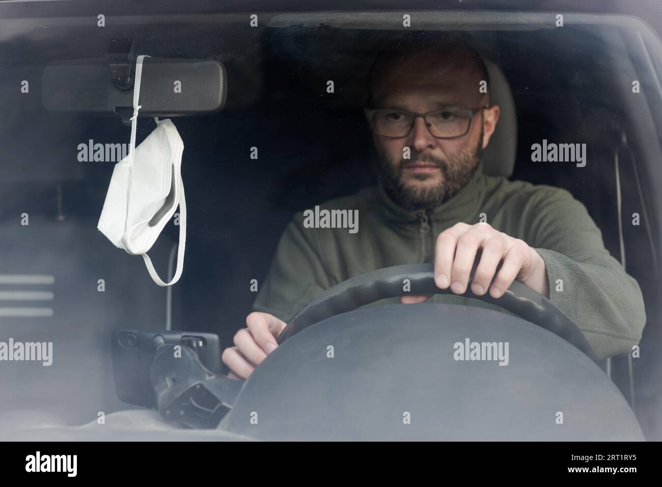 Portrait of young man sitting in car looking at protective face mask ...