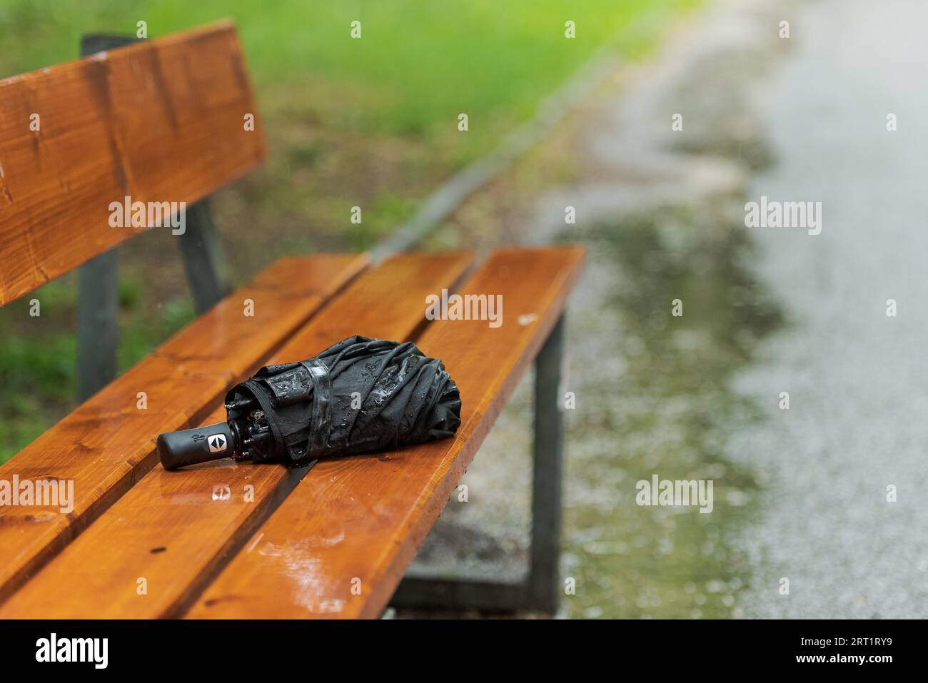 Forgotten black folded wet rain umbrella lying on wooden park bench ...