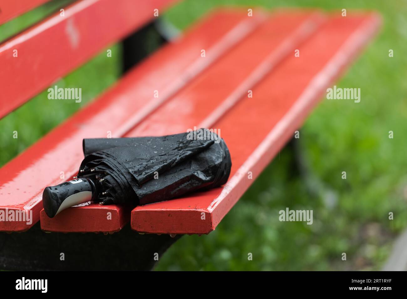 Forgotten black folded wet rain umbrella lying on wooden park bench ...