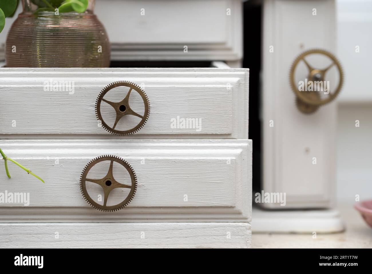 Detail of white miniature cupboard with toothed wheels as drawer knobs ...