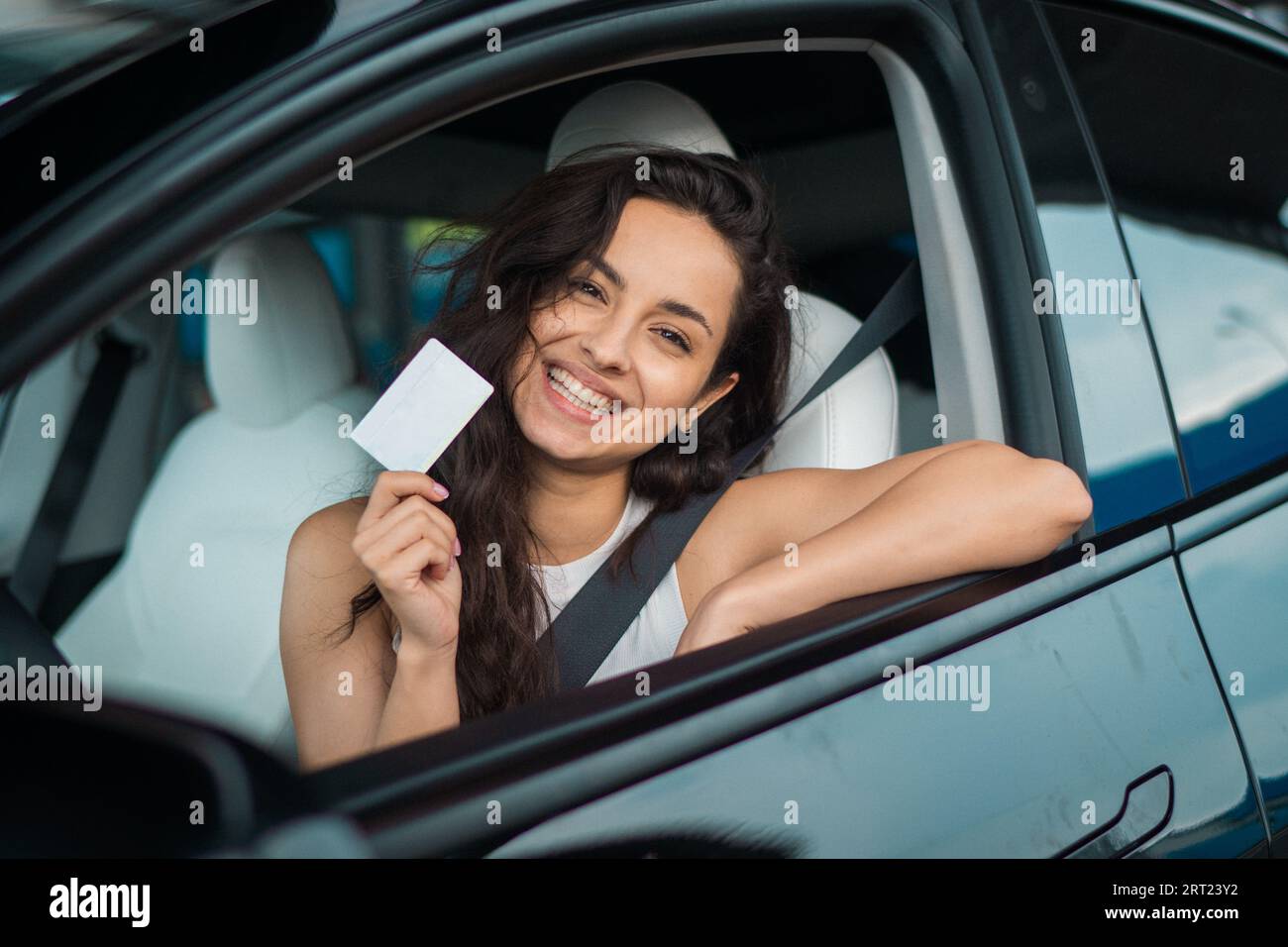 Happy cheerful young woman showing a driving license while sitting in ...