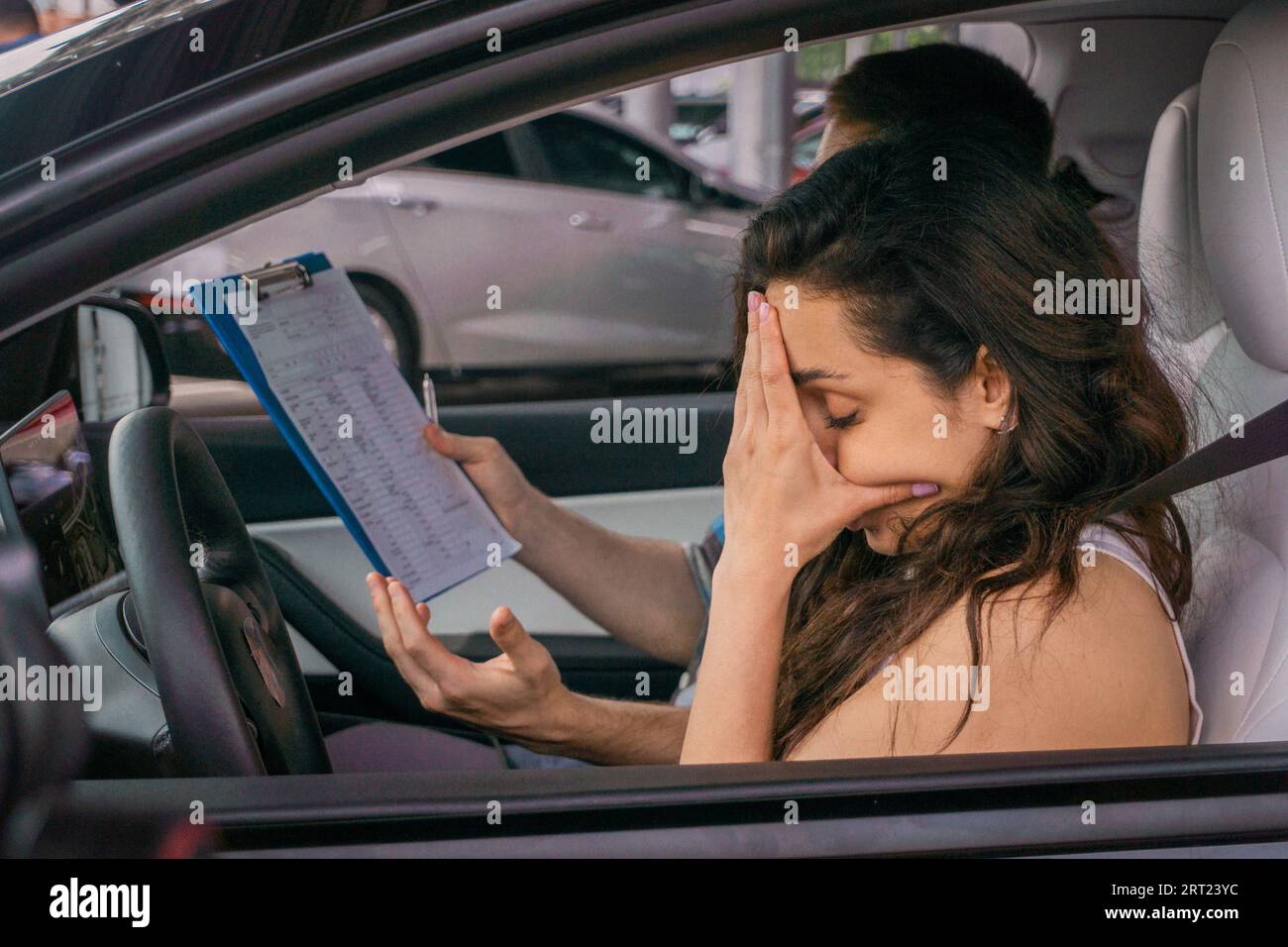 Tired young woman sitting in car covering face in hands, instructor ...