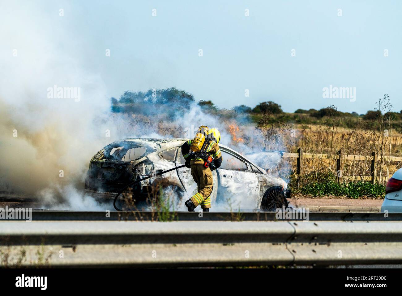 Fireman attending a car fire on a layby on a major road, A299 in the ...