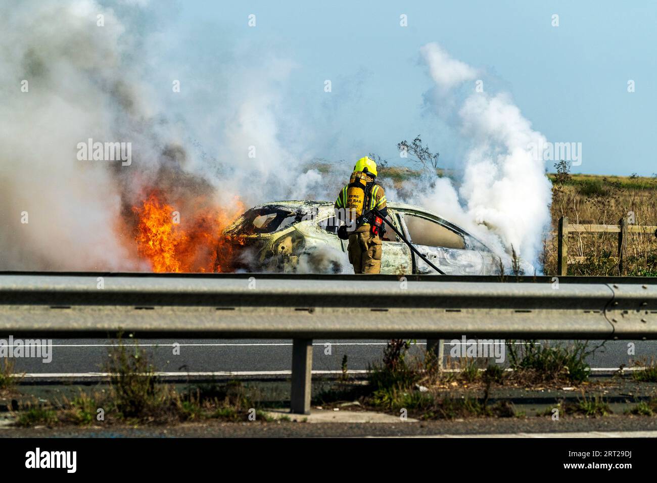 Fireman attending a car fire on a layby on a major road, A299 in the ...