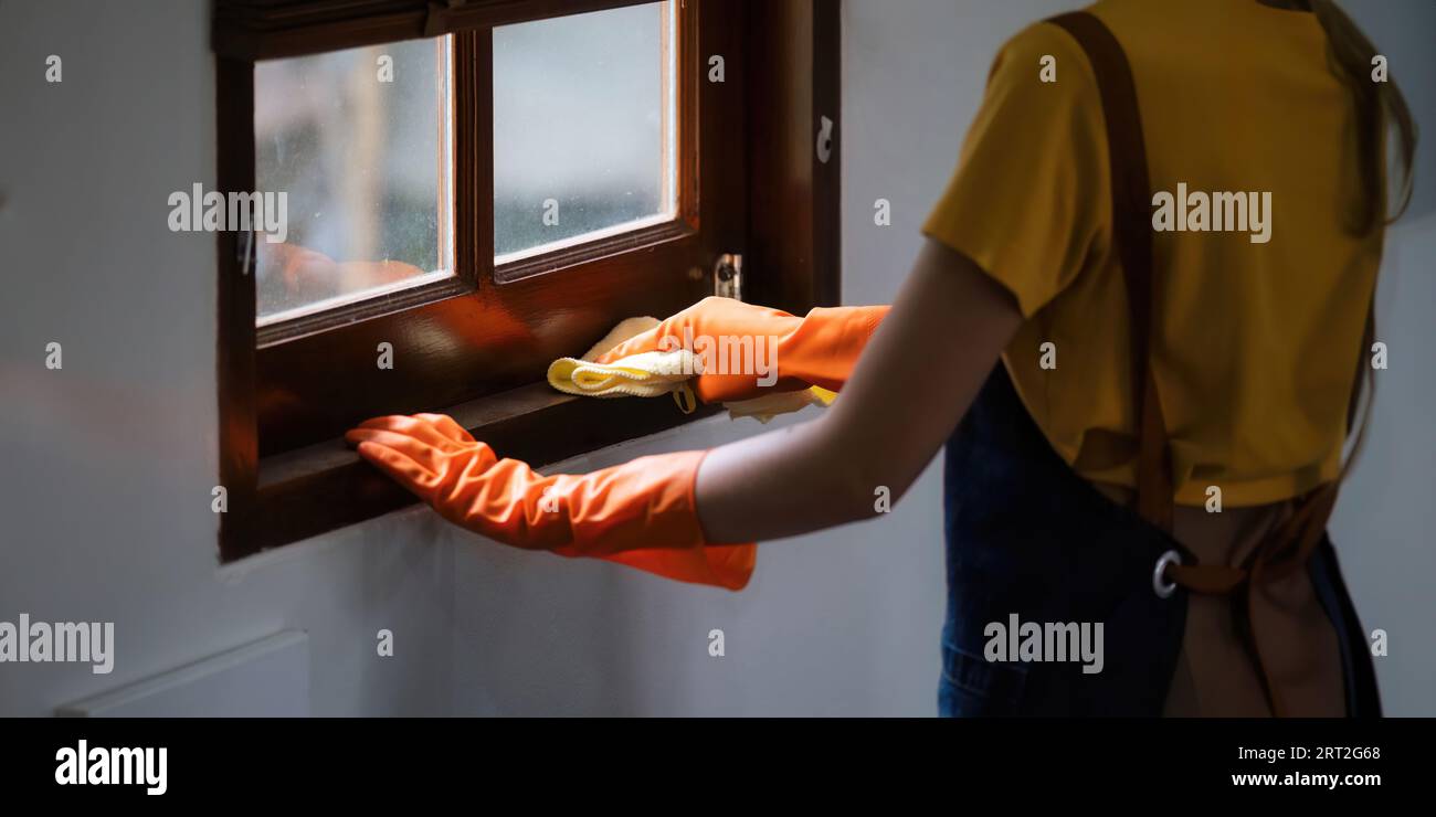 Housekeeper cleaning window sill with orange rag cleaning service ...