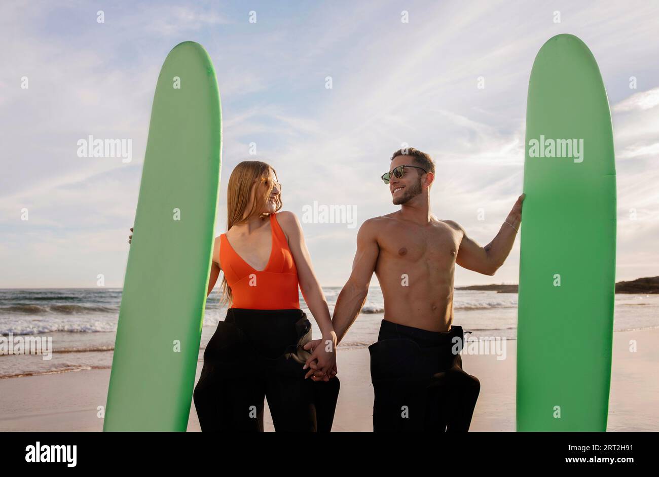 Young Surfers Couple Holding Hands And Posing With Surfboards On The