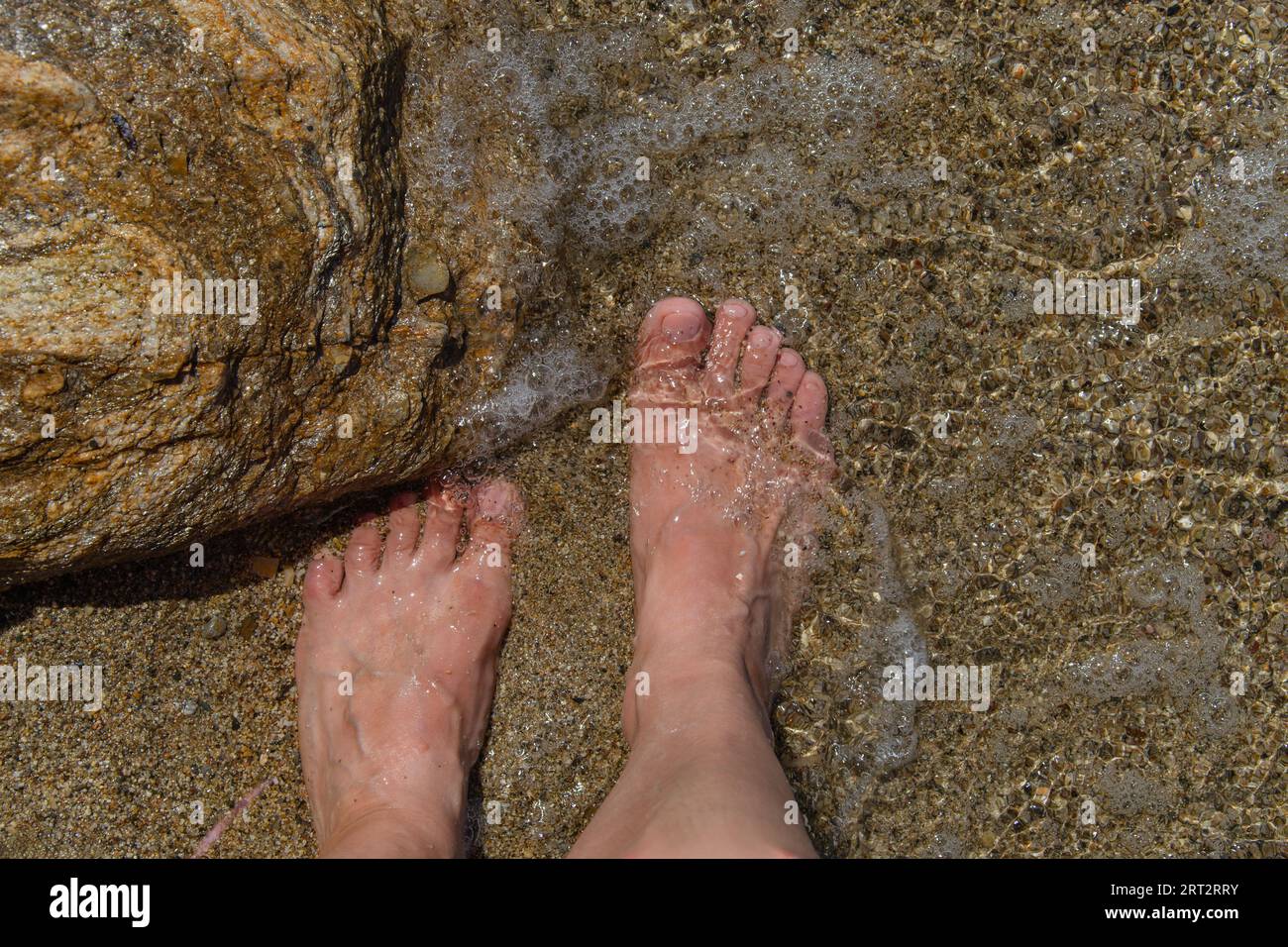 Barefoot women's feet close-up in clear water on the sandy bottom next ...