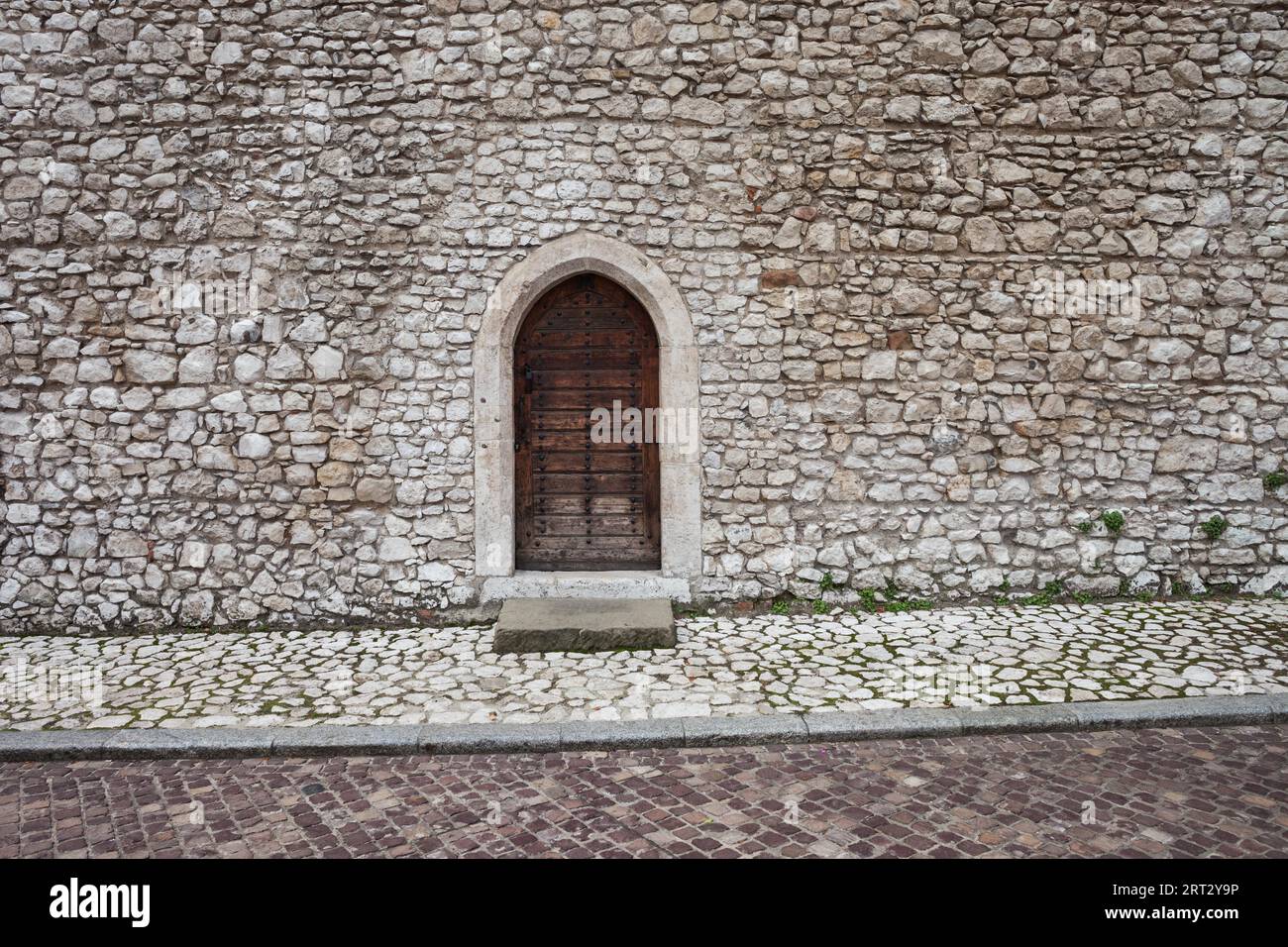 Medieval castle stone wall with arched wooden door and sidewalk Stock ...
