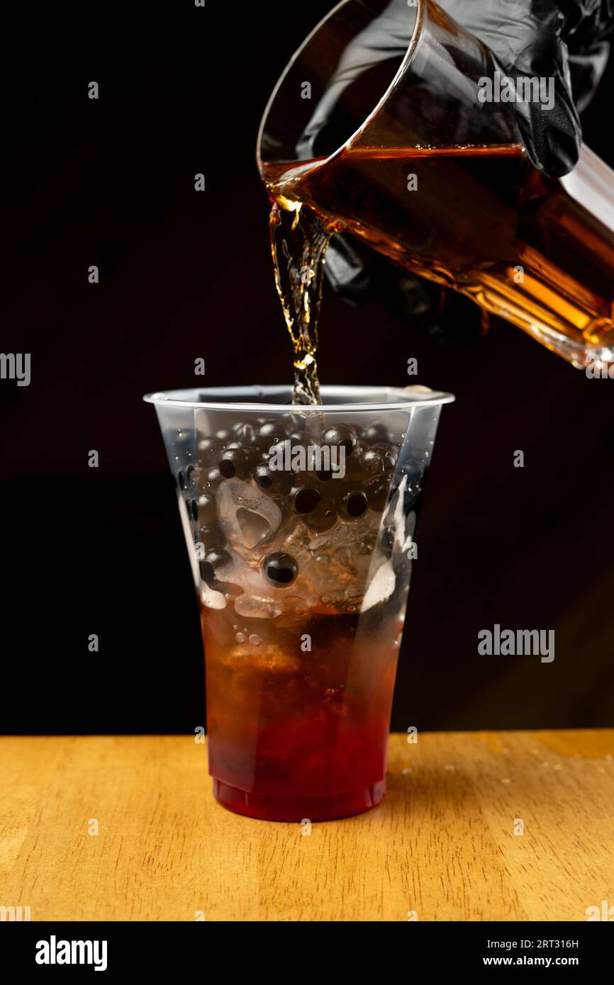 Making milk bubble tea with tapioca pearls, pouring tea in a plastic ...