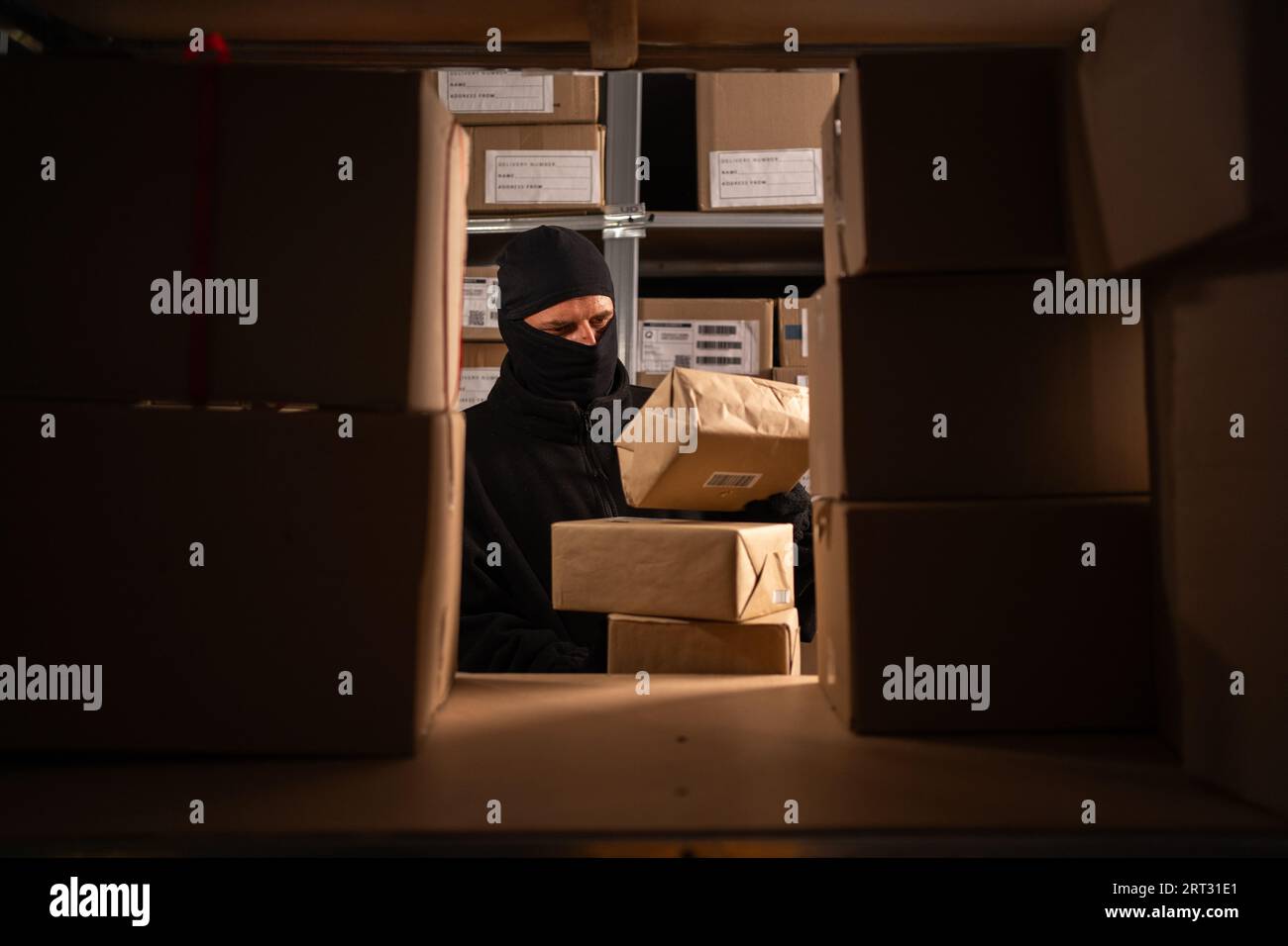 Thief in black balaclava steals with a parcel in a warehouse at the ...