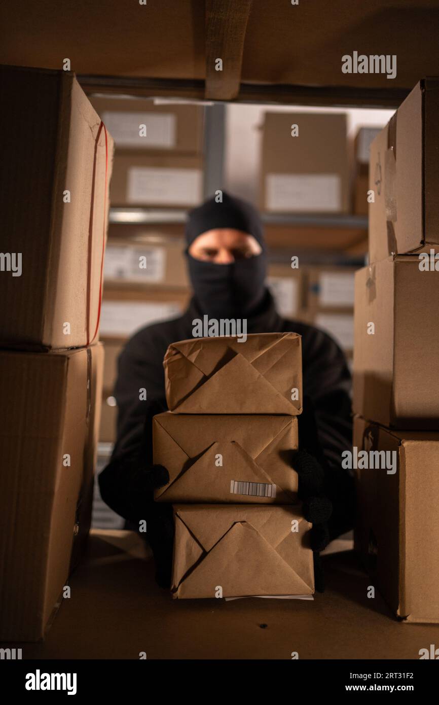 Thief wears gloves steal boxes of goods in a warehouse in the dark ...