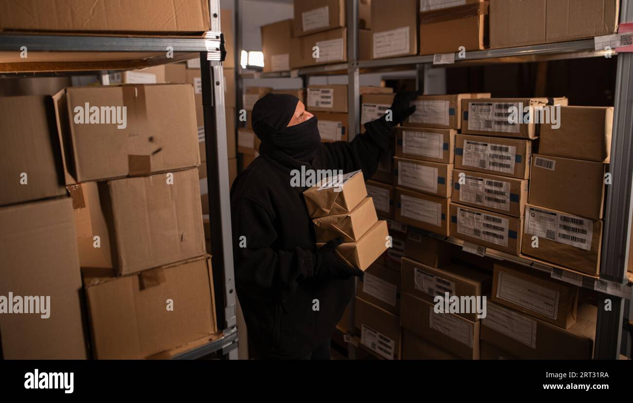 Thief wears gloves steal boxes of goods in a warehouse in the dark ...