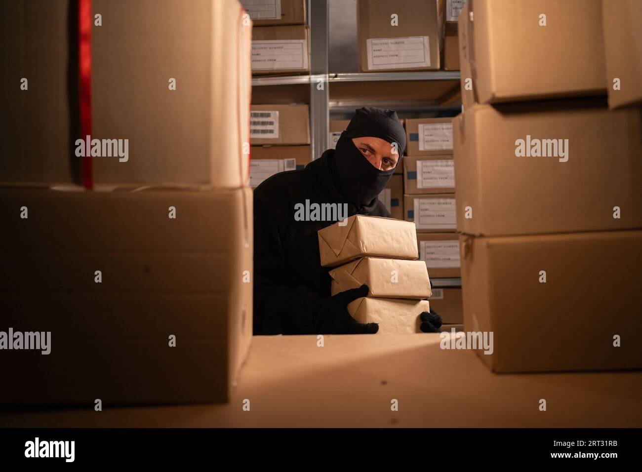 Thief in black balaclava steals with a parcel in a warehouse at the ...