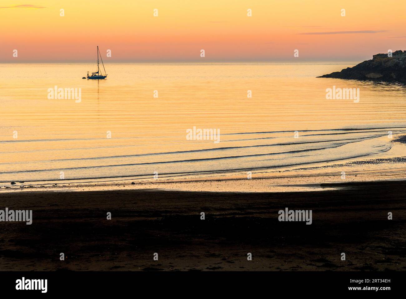 A yacht at anchor at sunset on the north coast of Anglesey at Cemaes in ...