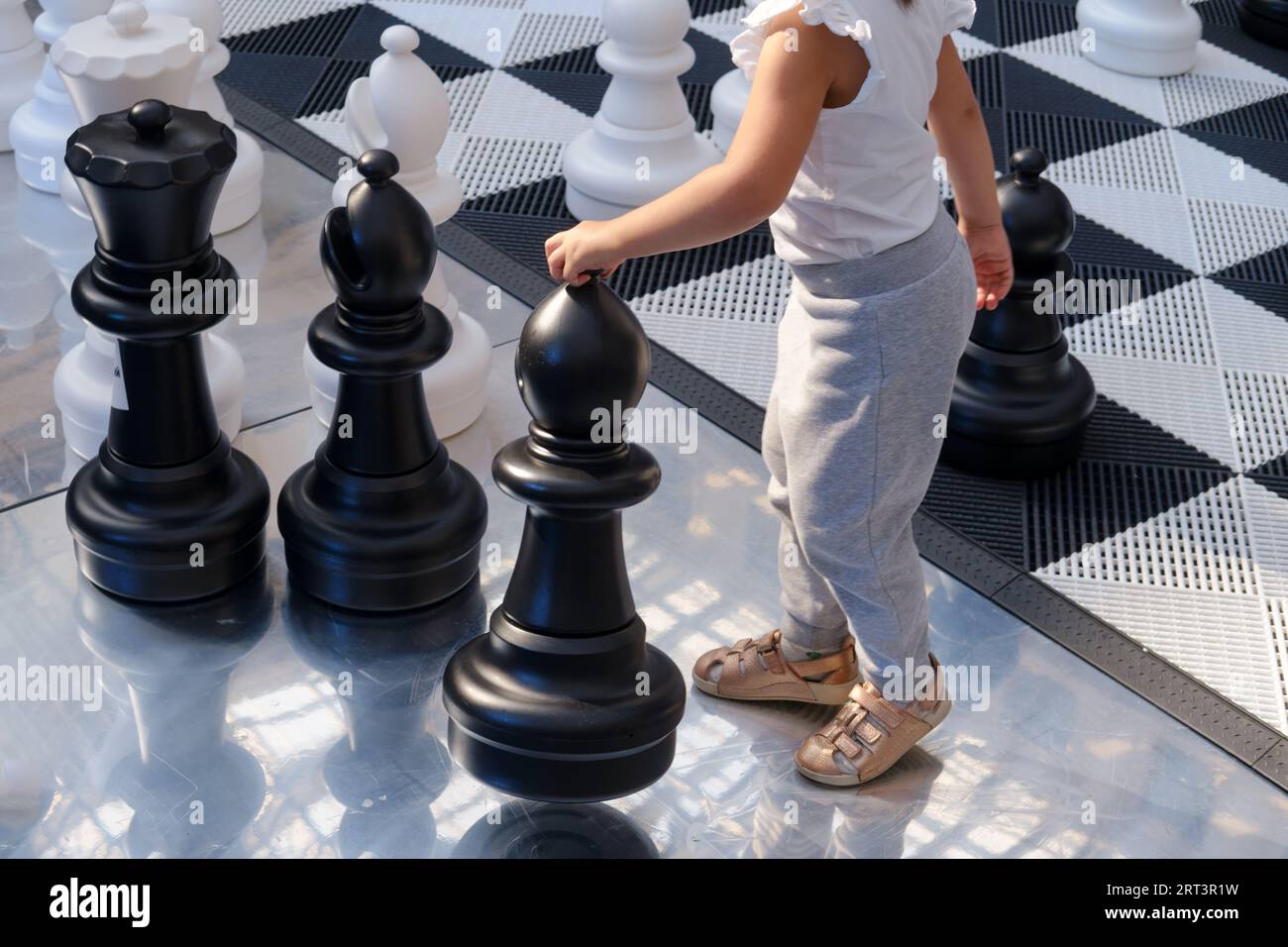 Little girl playing big chess on a large chessboard with black and ...