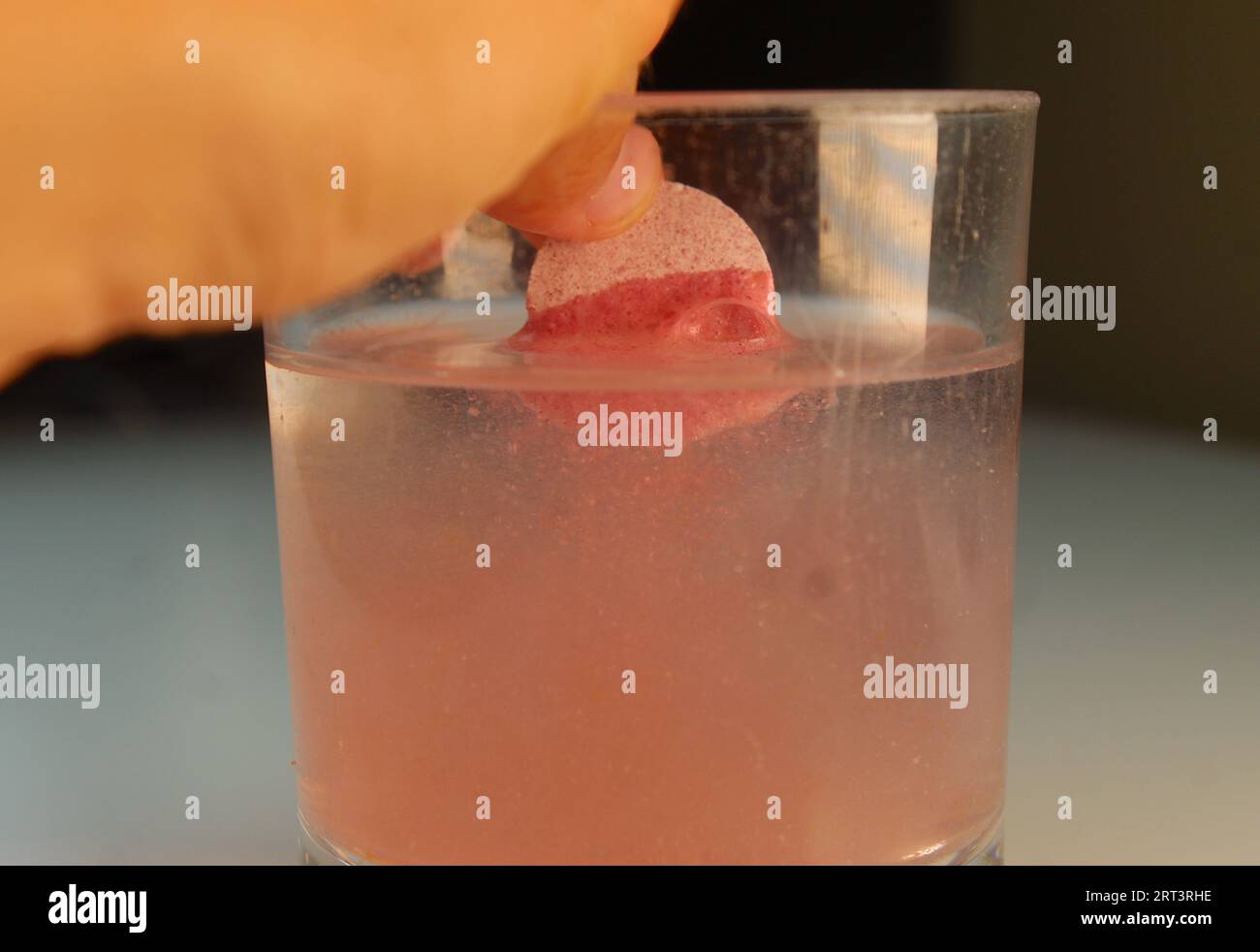 A photo of a pink electrolyte tablet dissolving in a glass of water ...