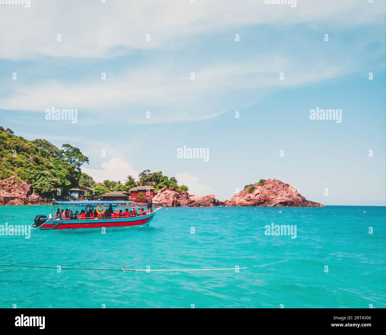 A small red wooden boat is pictured afloat in a calm body of water near ...