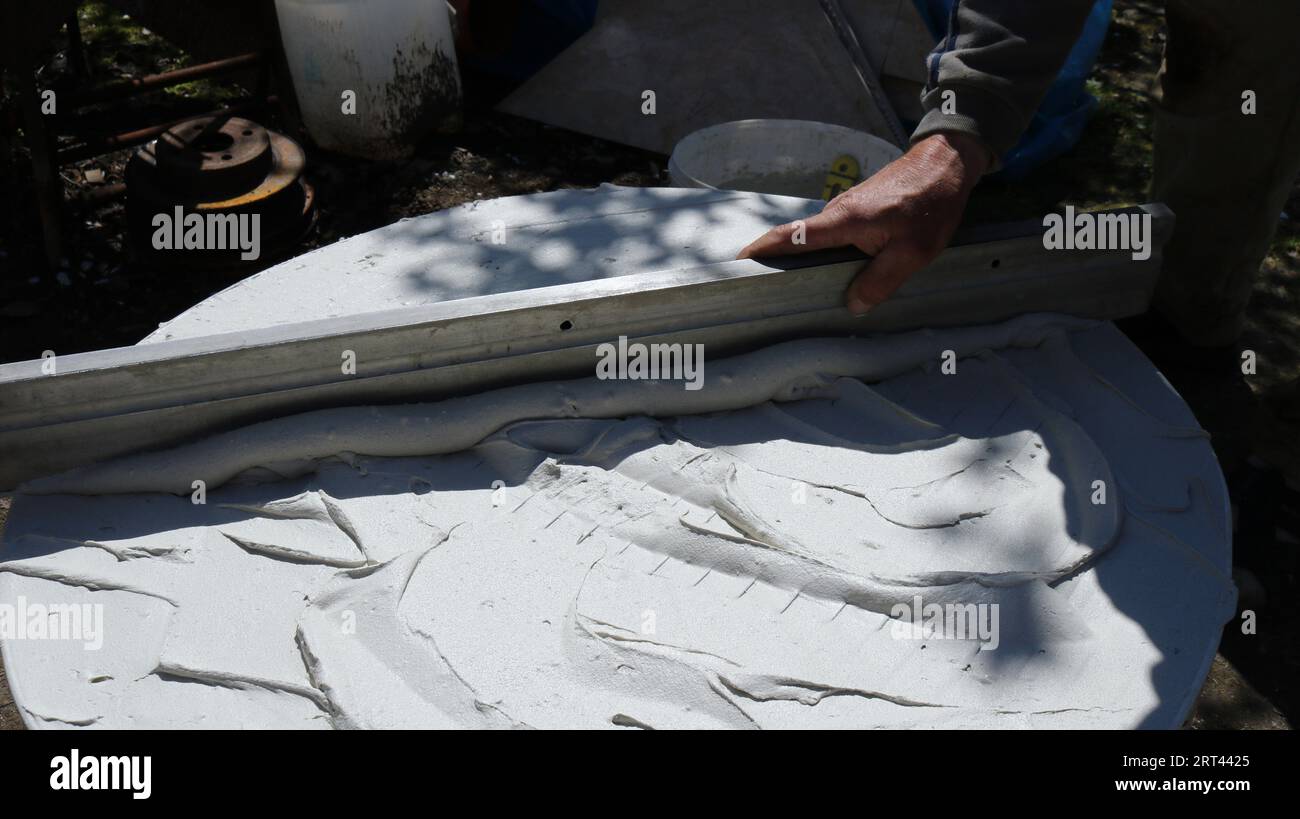 leveling a layer of mastic on a round surface using a flat long beam, a ...