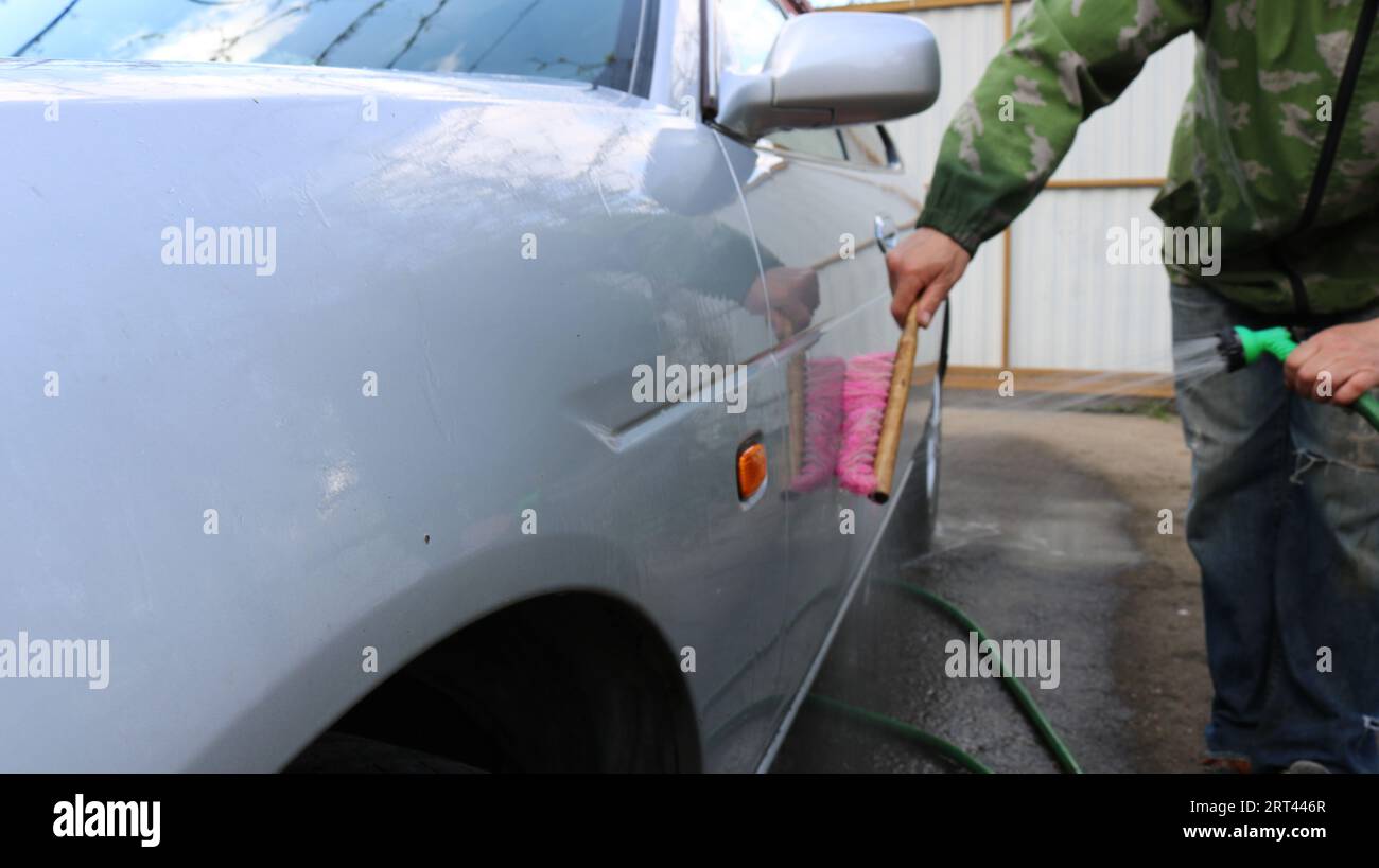 man washing the body of a gray car with a pink brush and a green hose ...