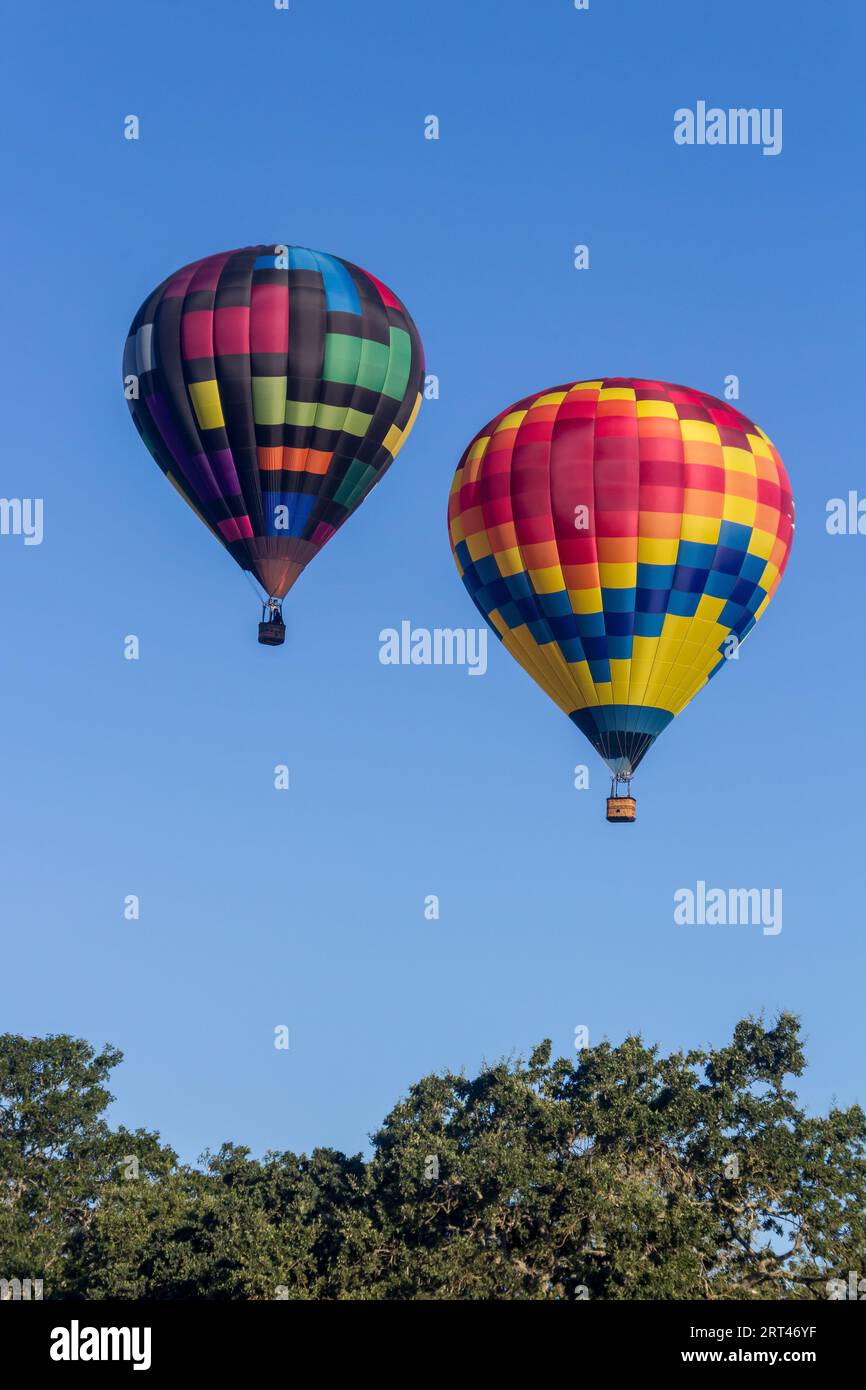 2 hot air balloons are rising in the early morning light into a blue ...