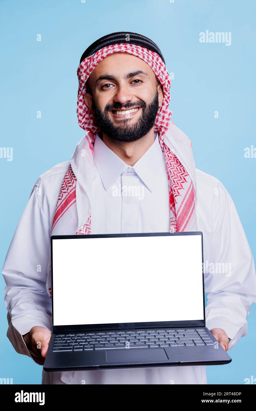 Smiling muslim man showing laptop with blank screen mockup for software ...