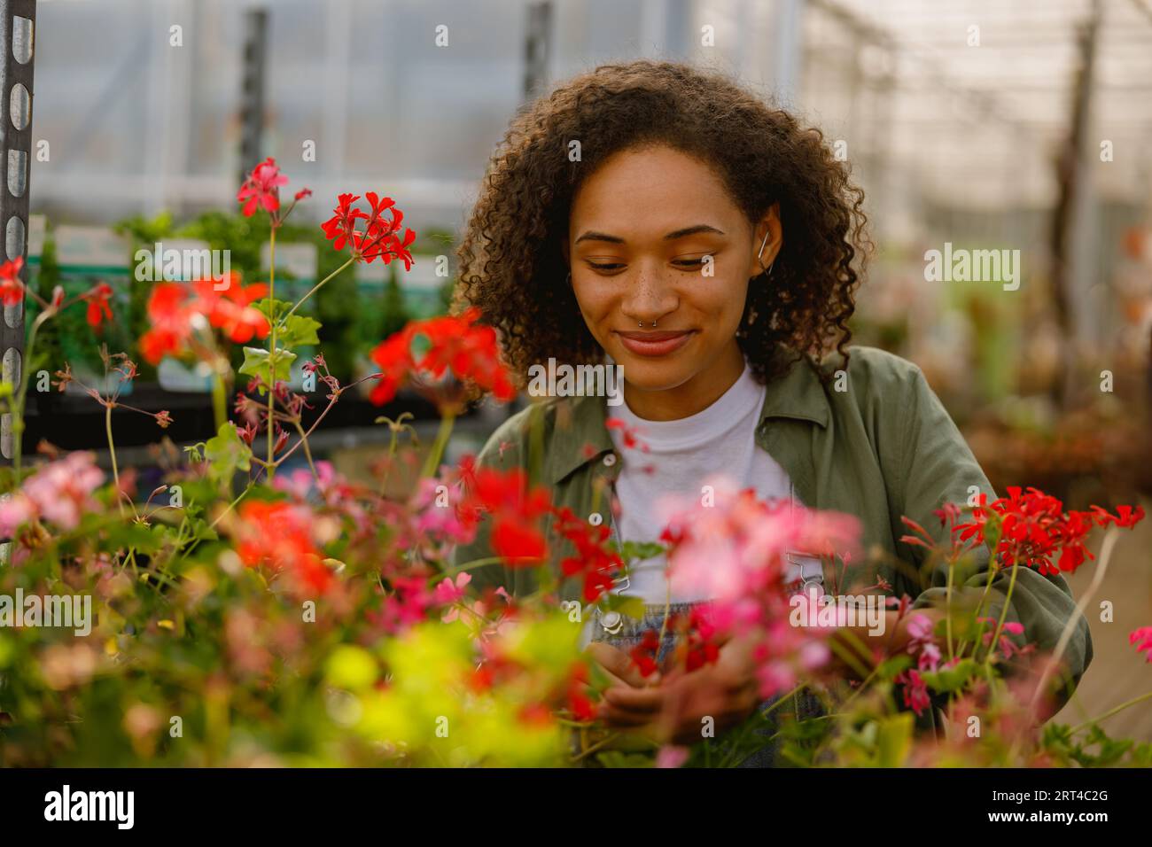 Smiling female gardener working with plants while standing on ...
