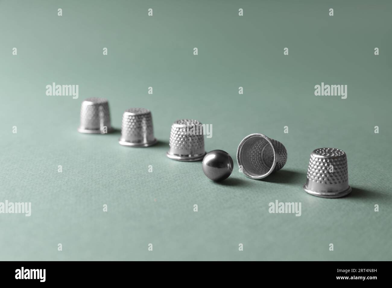 Metal thimbles and ball on pale olive background. Thimblerig game Stock ...