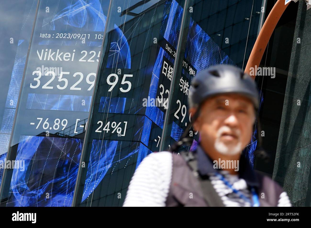 A person rides a bicycle in front of an electronic stock board showing ...