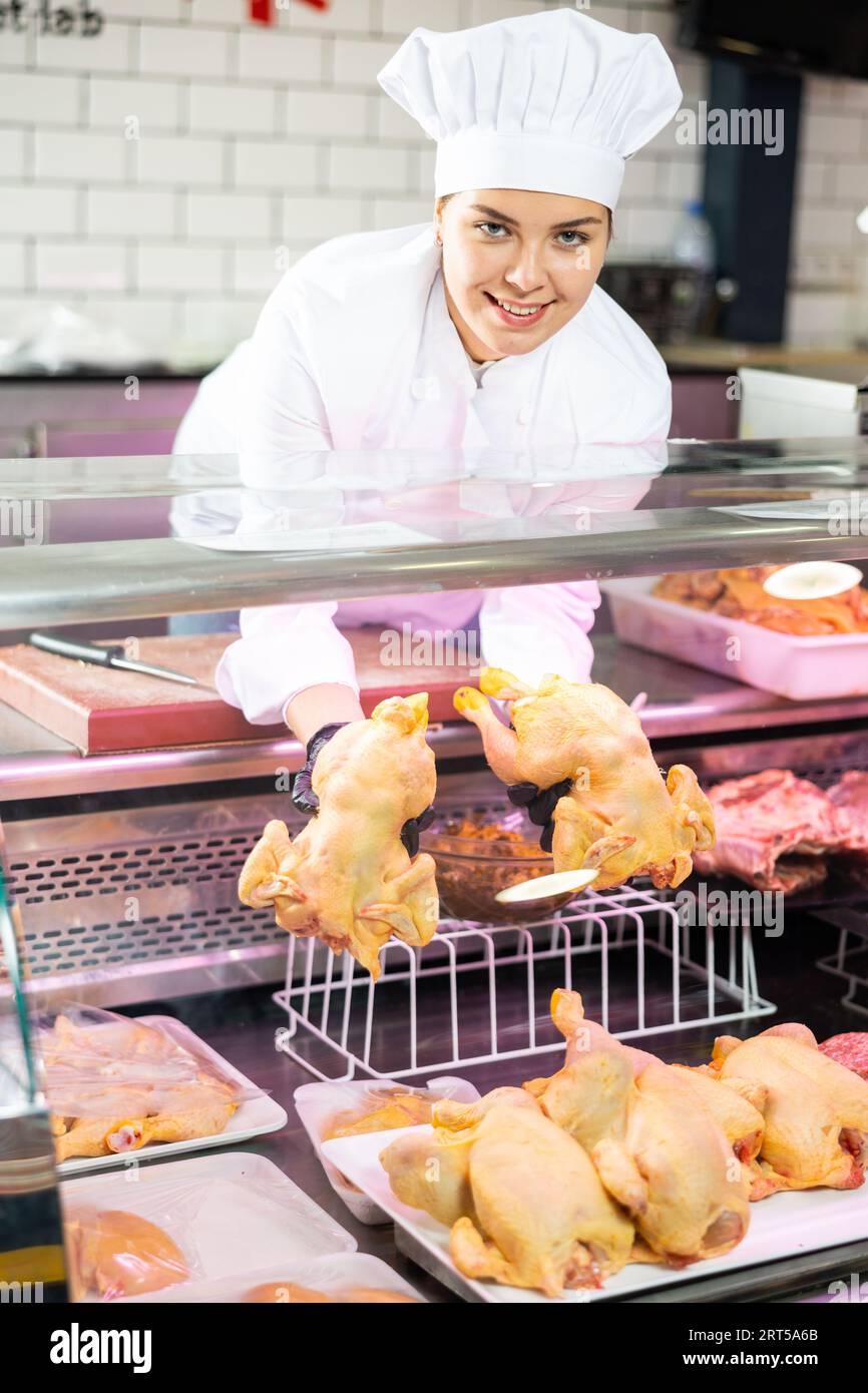 Female butcher laying broiler chickens in display case Stock Photo - Alamy