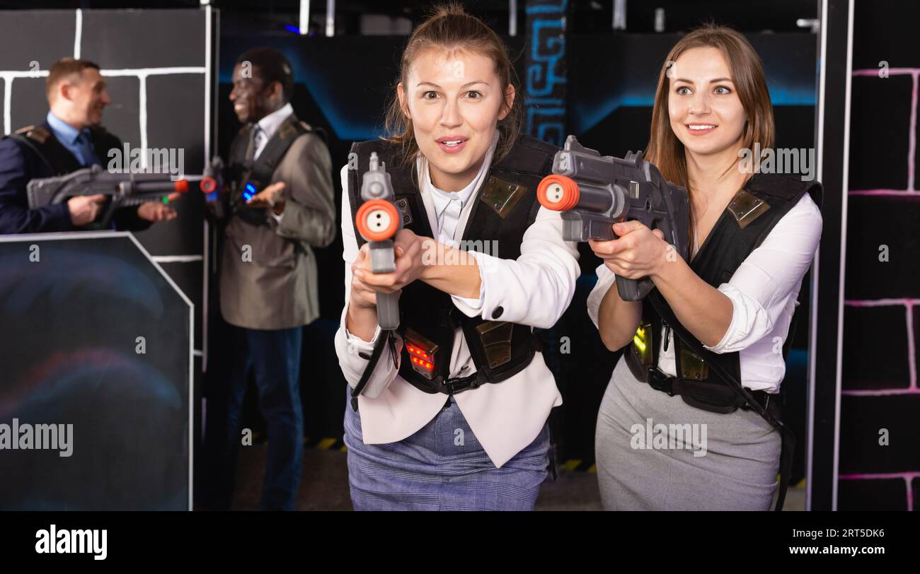 Portrait of two women in business suits playing laser tag with co ...