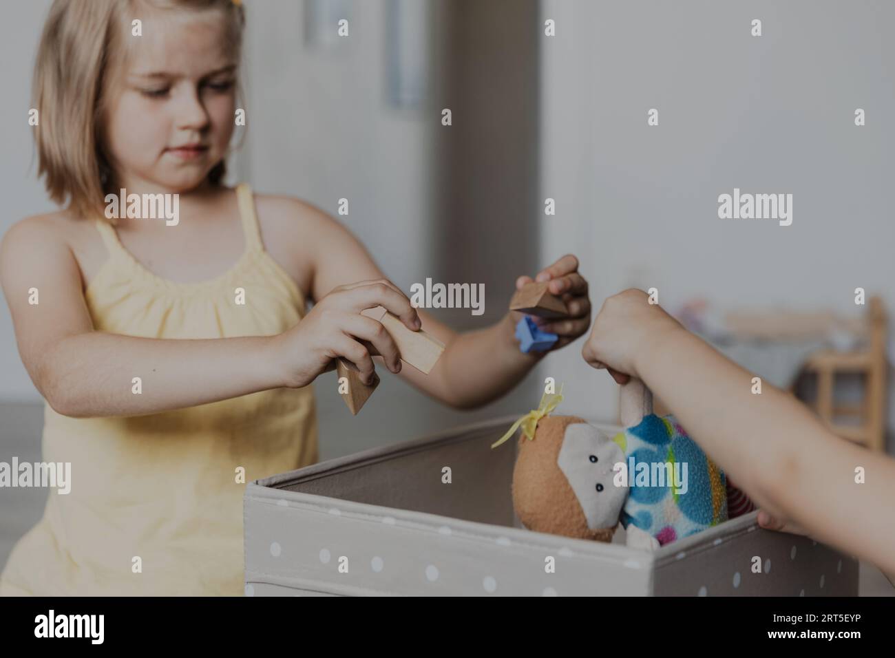 Children cleaning toys from floor after playing, sister helping to ...