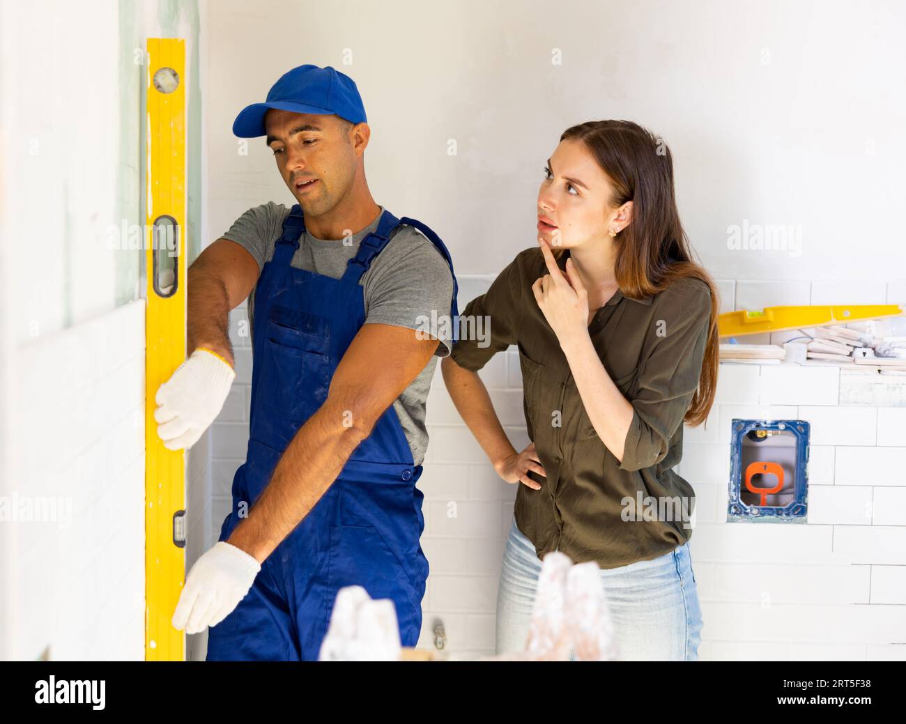 Woman watching repair man measuring wall with spirit level Stock Photo ...