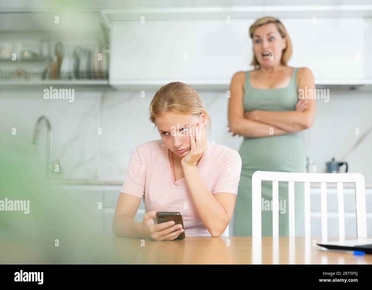 Upset teenage girl sitting with phone while disapproving mother ...