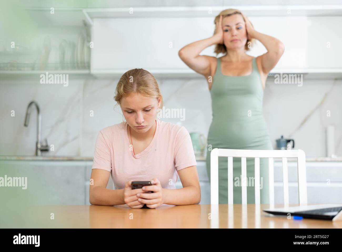 Upset teenage girl sitting with phone while disapproving mother ...