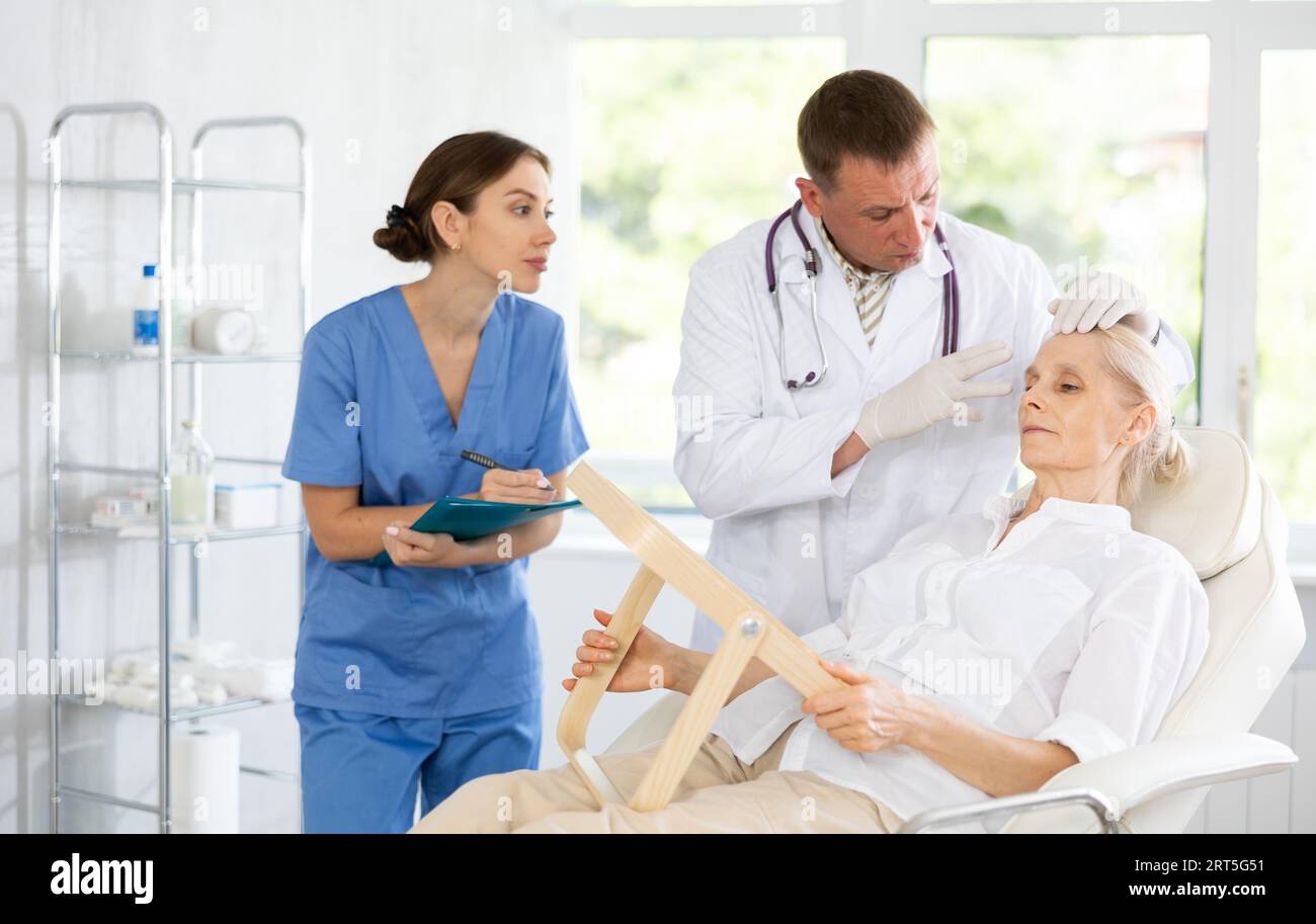 Man dermatologist examines skin of senior womans face, female nurse ...