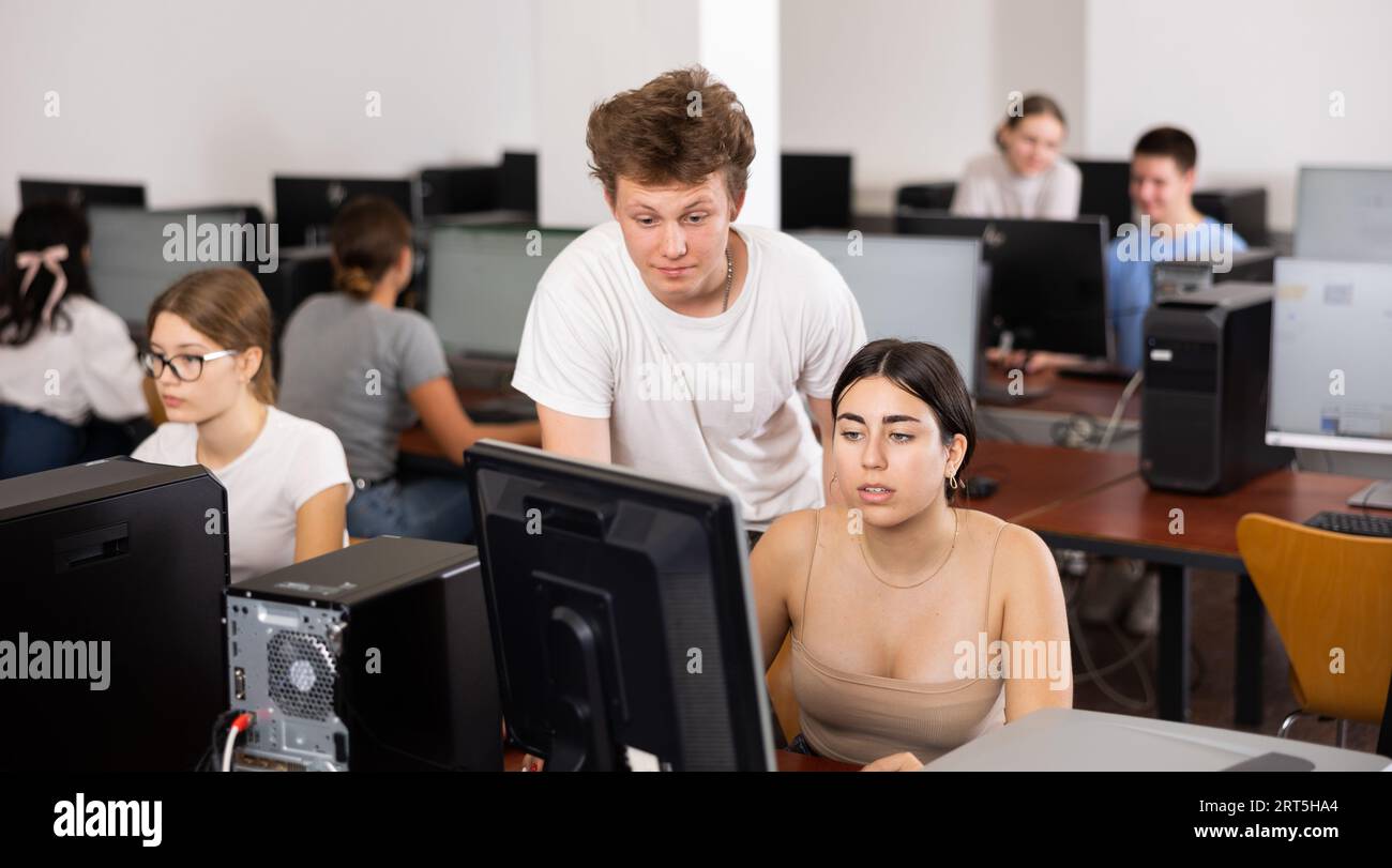 Teenage students working together at desk using computer on media ...