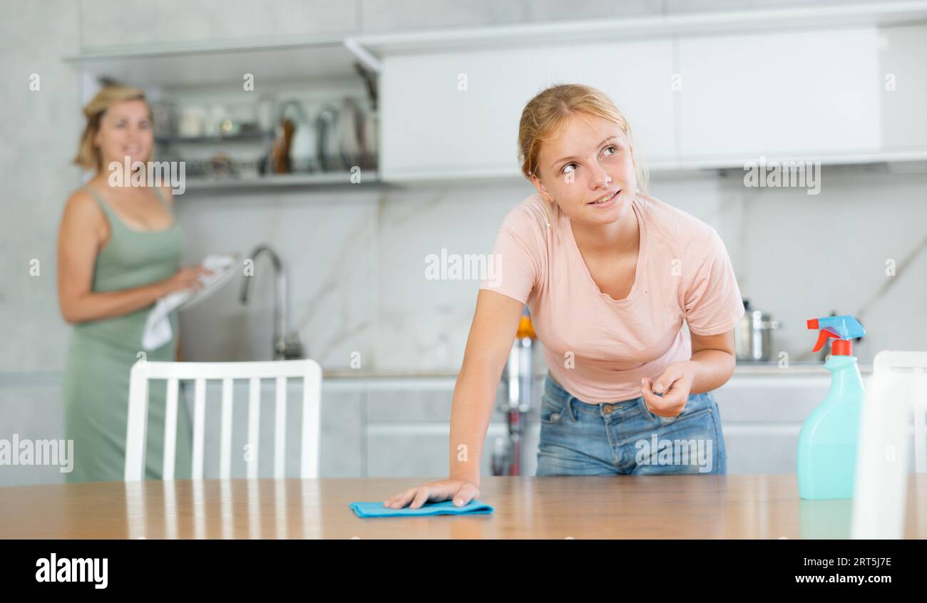 Teen girl help mother and wash dining table in kitchen, blurry mom ...
