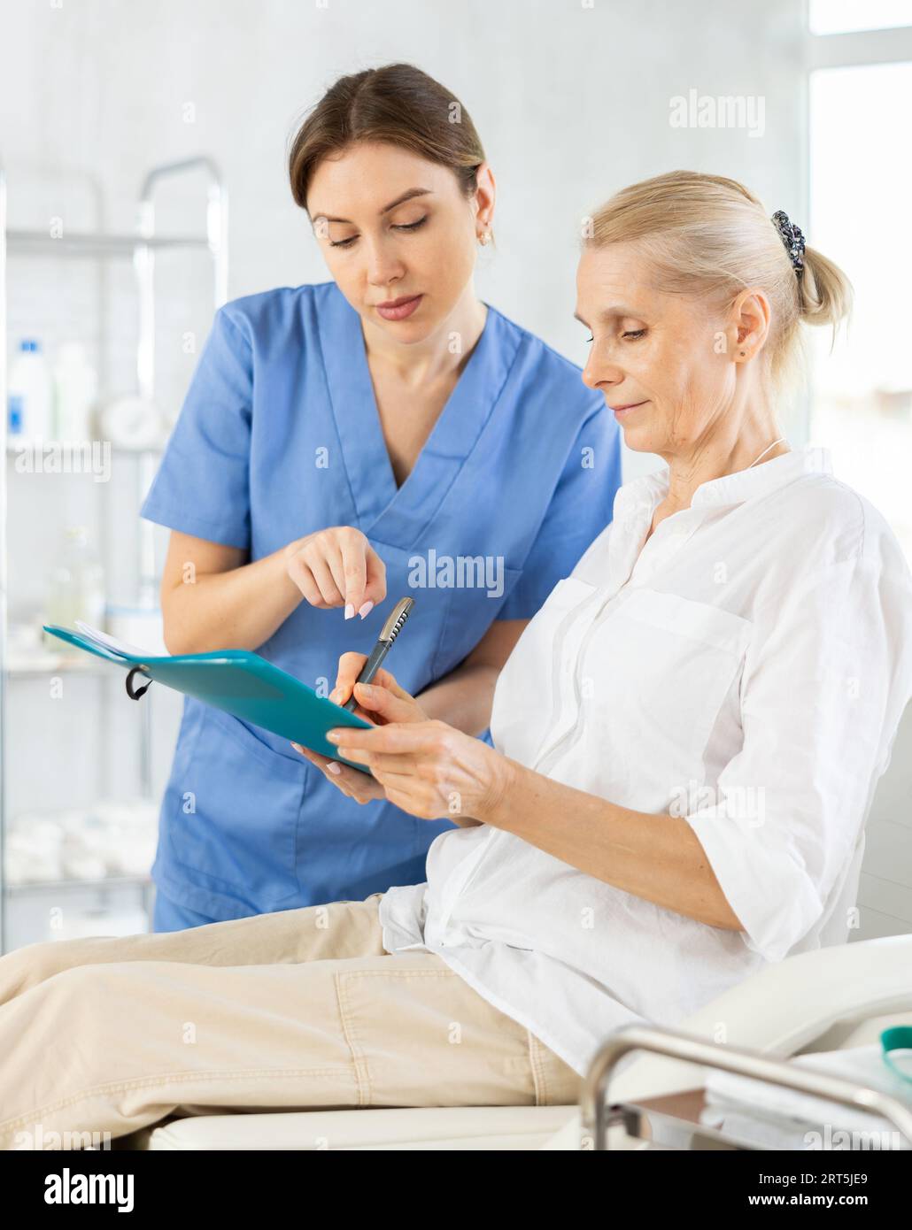 Old female patient signing document while talking with woman doctor ...