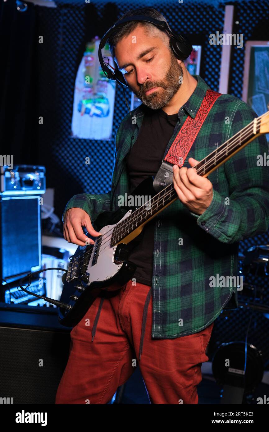 Musician man playing electric bass with headphones at home recording ...