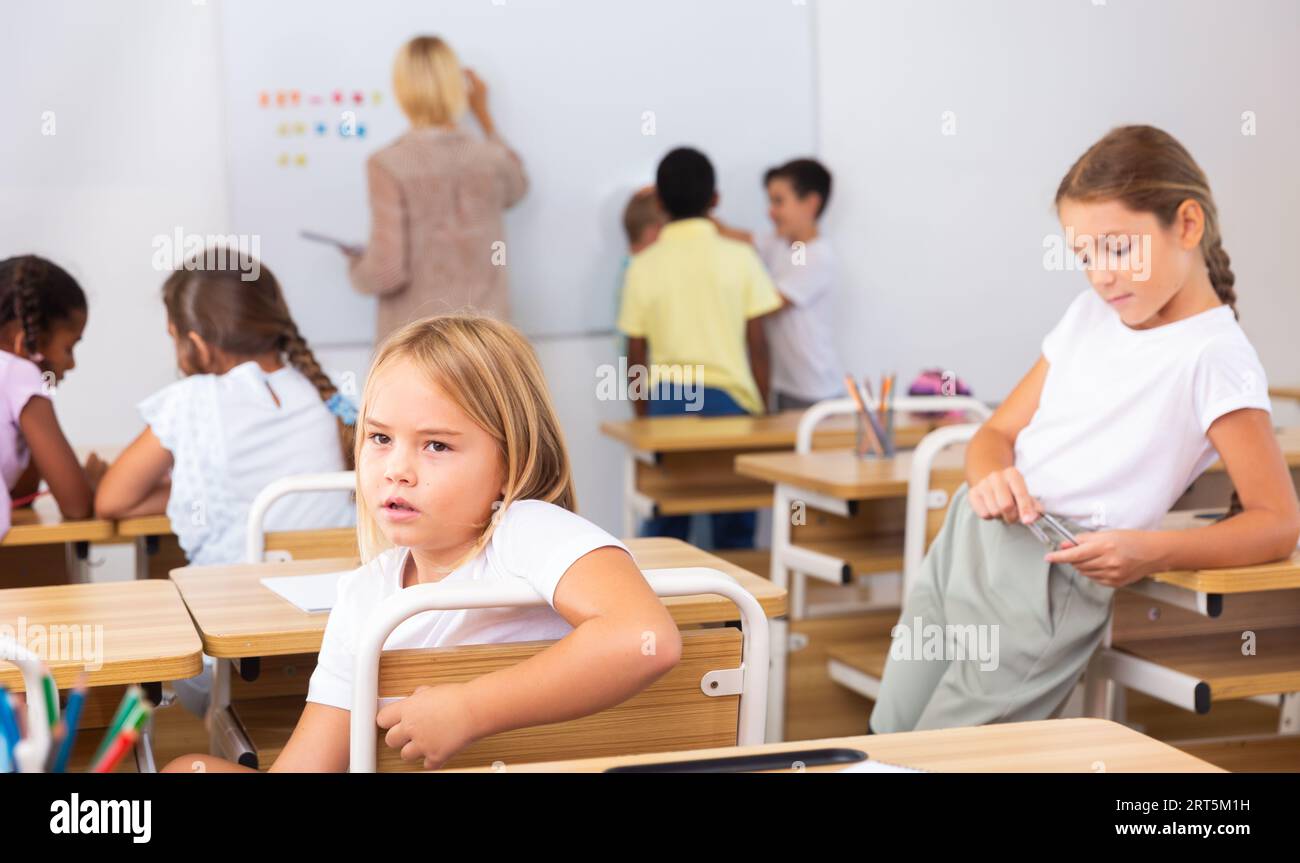 Happy preteen schoolchildren communicating during recess in classroom ...