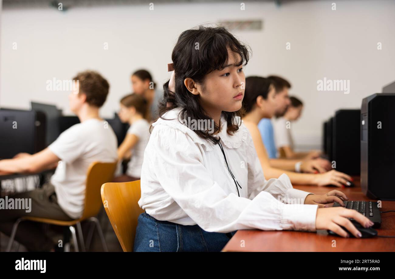 Portrait of fifteen-year-old schoolgirl studying at computer in class at an informatics lesson ...