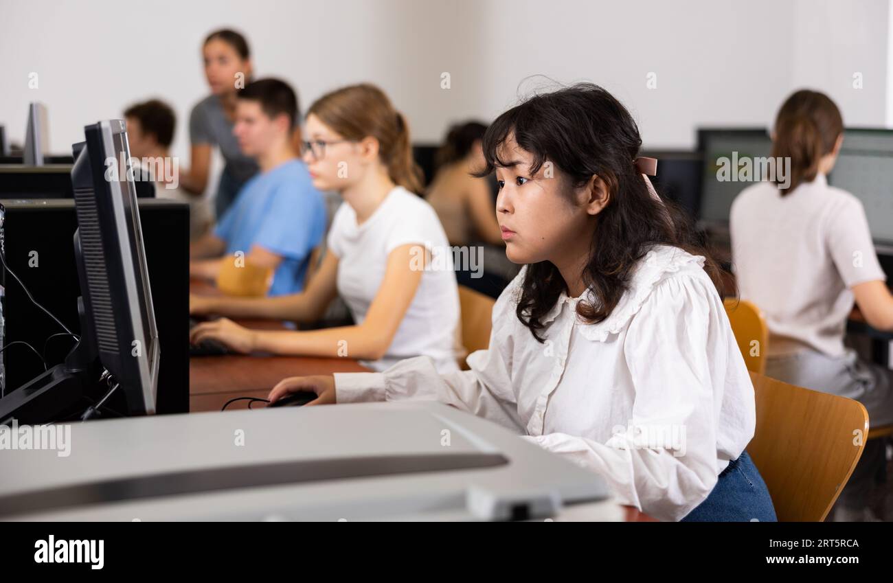 Portrait of fifteen-year-old schoolgirl studying at computer in class ...