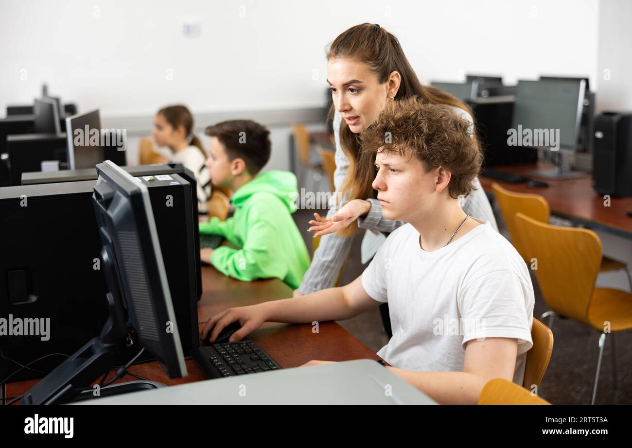 Female teacher helping focused teenage student in computer lab Stock ...
